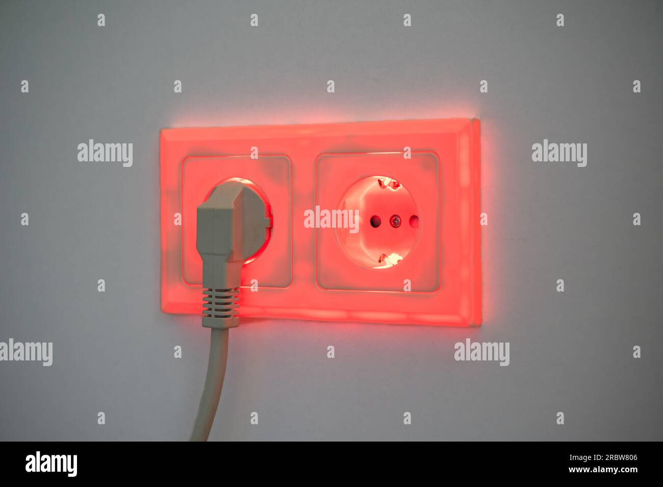 Red illuminated socket with plug inserted to symbolise power ...