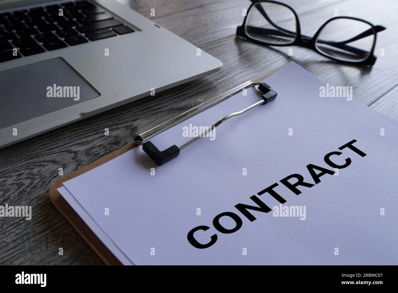 Paper clipboard with text CONTRACT on table with laptop and glasses ...