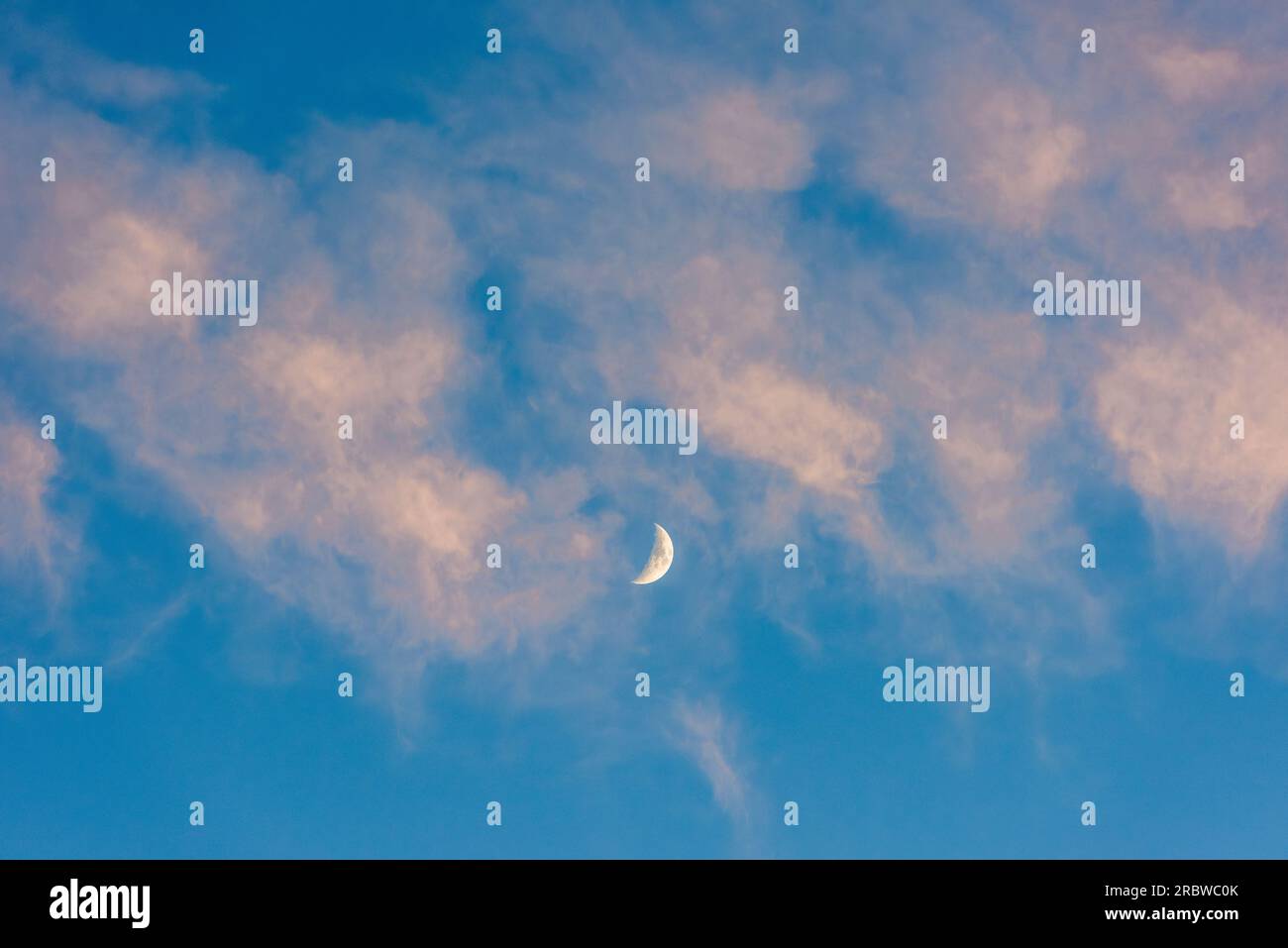 An evening sky with a waxing crescent moon showing through pink sunset ...