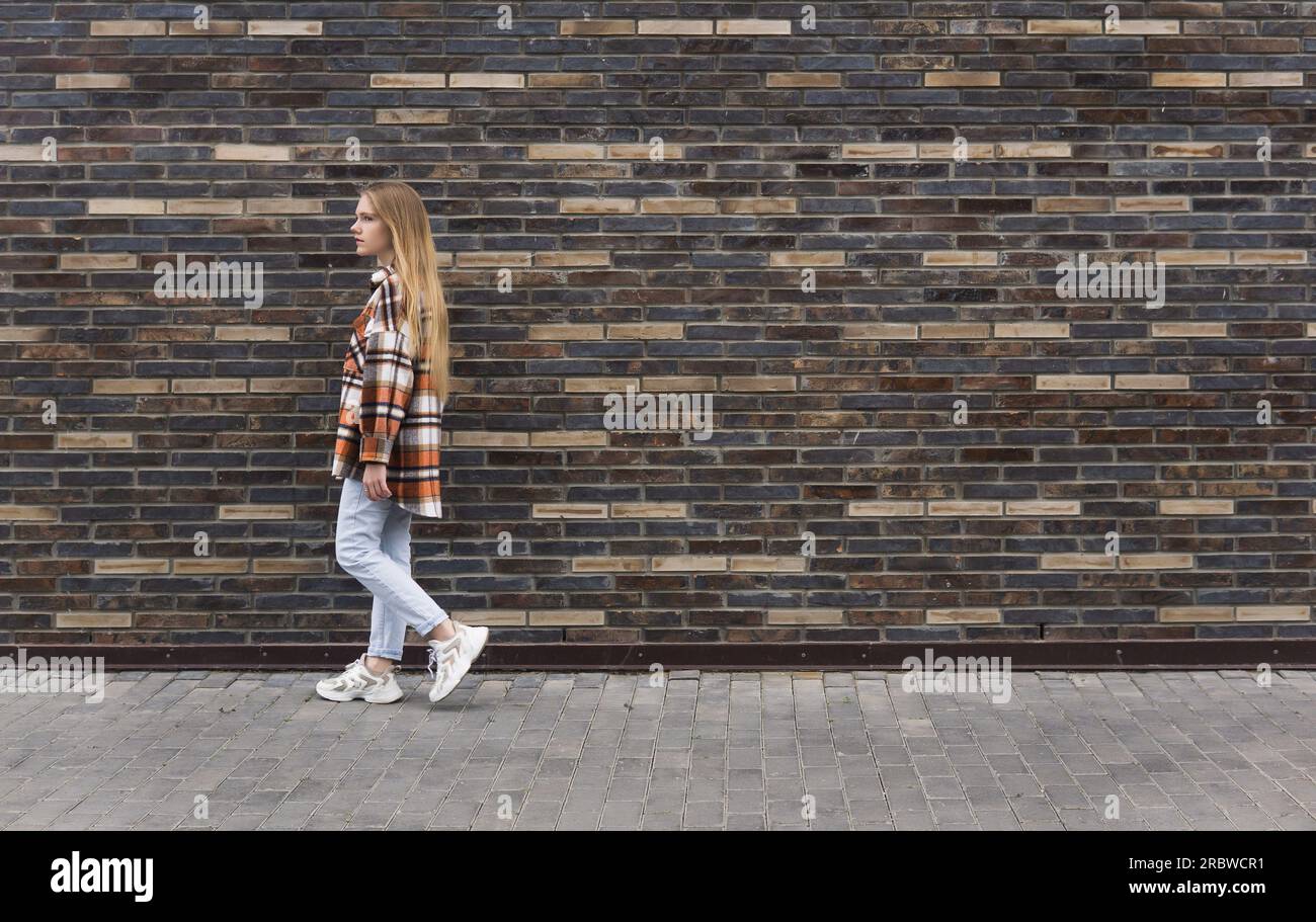 young woman walks down the street in front of a brick wall Stock Photo ...