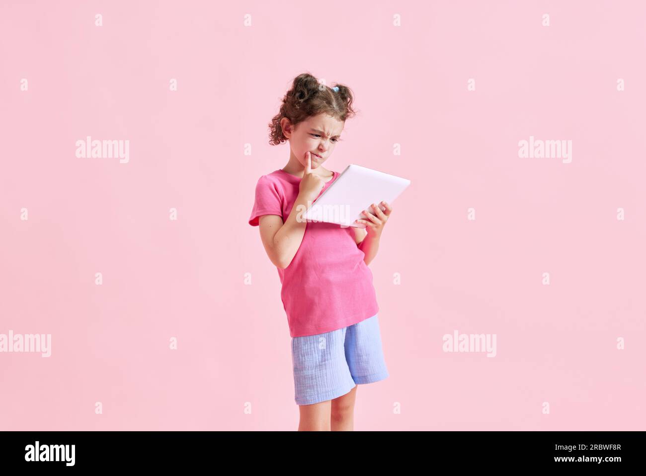 Portrait of child, little girl looking in tablet with thoughtful ...