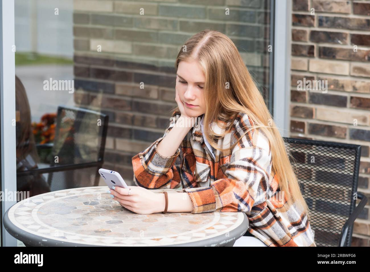 young woman reading something on the phone while sitting at an outdoor ...