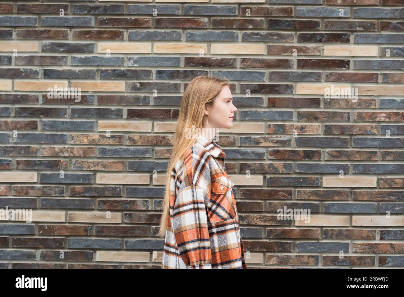 young woman walks down the street in front of a brick wall Stock Photo ...