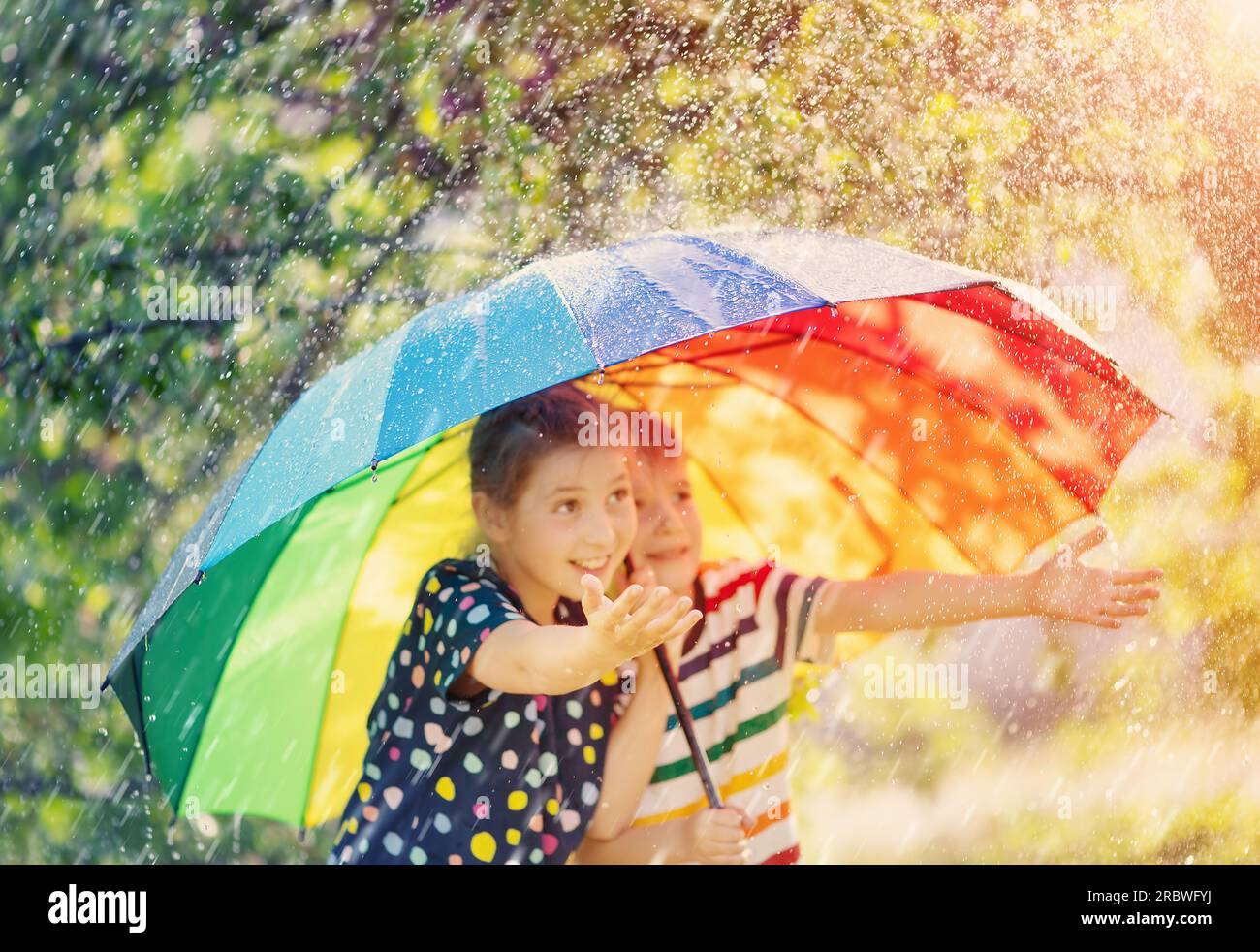 Boy and girl standing outdoors in rainy day under colourful umbrella ...