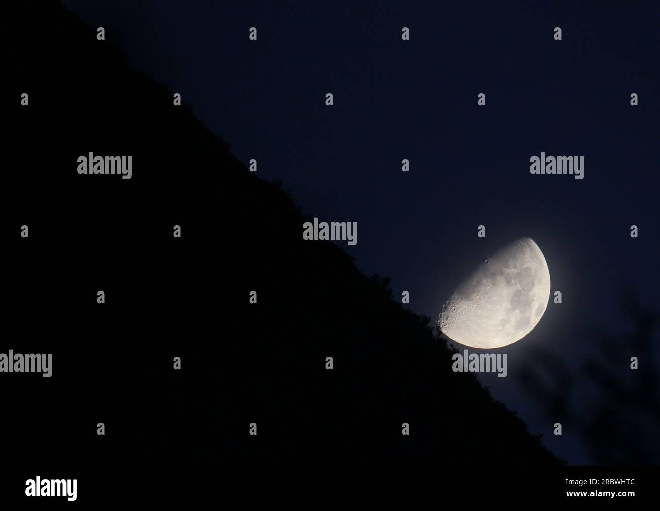 Partial moon on dark blue with slightly visible horizon in unusal angle ...