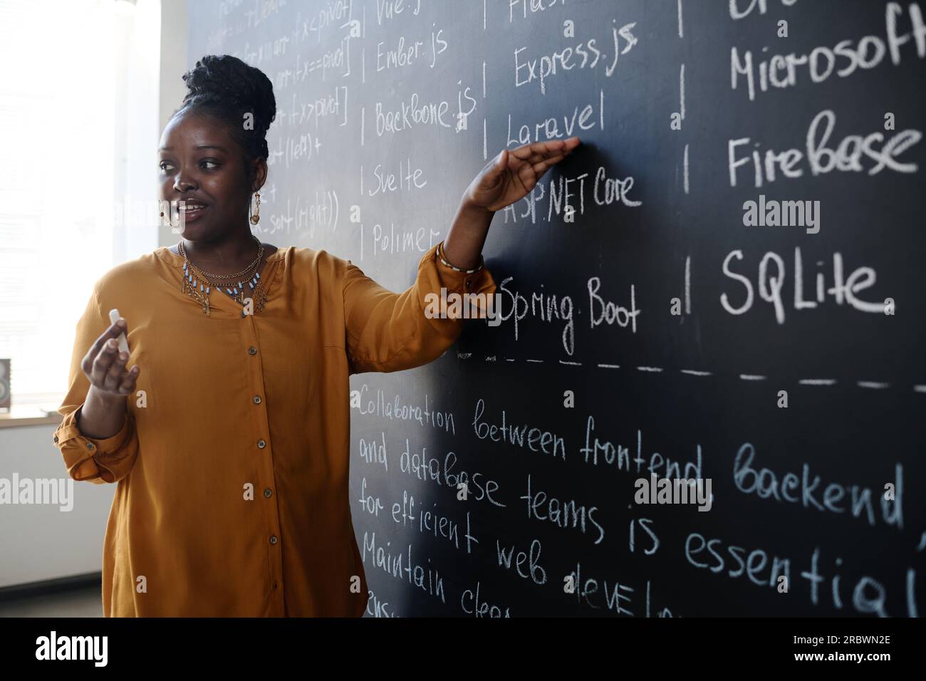 African American teacher pointing at blackboard and teaching IT lesson ...