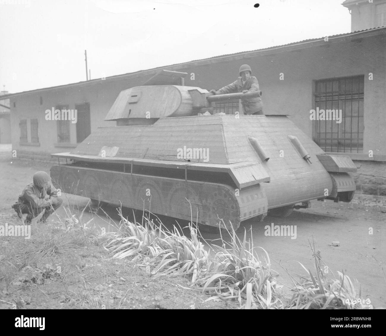 Two American soldiers inspect a wooden replica of a German tank mounted ...
