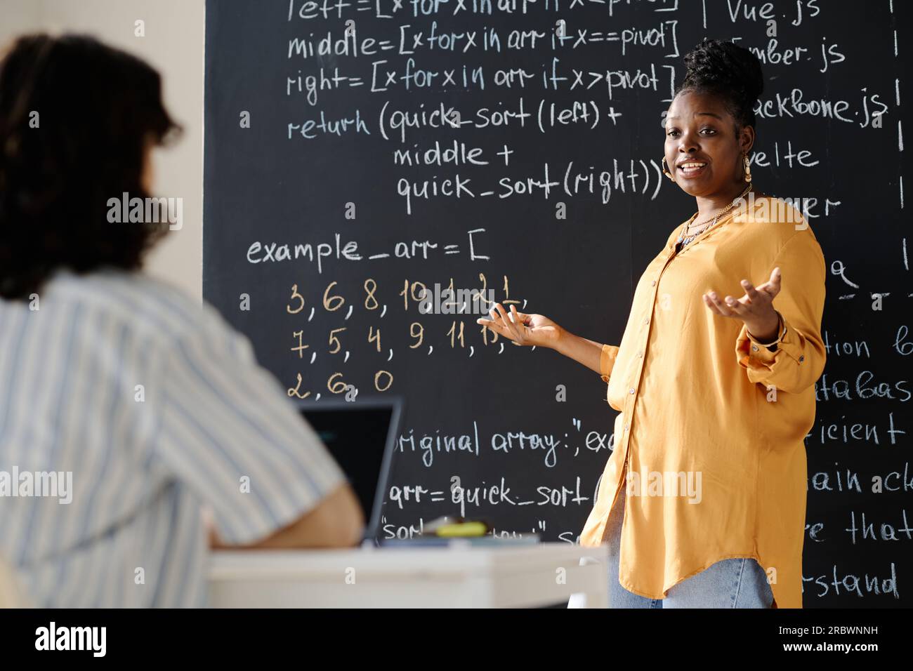 African American tutor standing near the blackboard and explaining IT ...