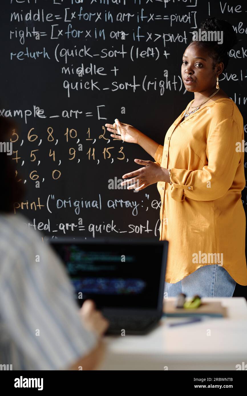 Vertical image of African American tutor pointing at blackboard and ...