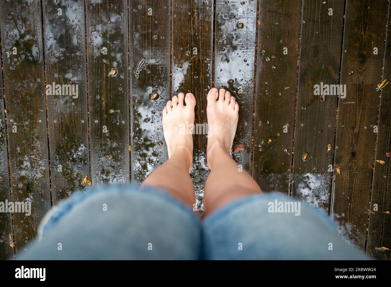 Person barefoot legs standing on wet wooden floor of patio at raining ...