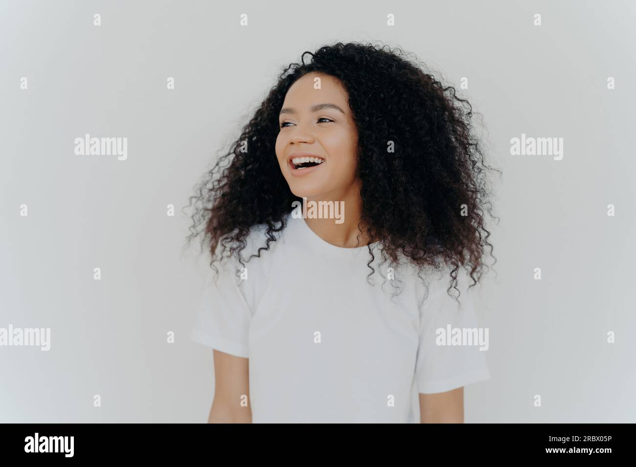 Beautiful curly woman, glad expression, smiles, laughs at funny moment ...