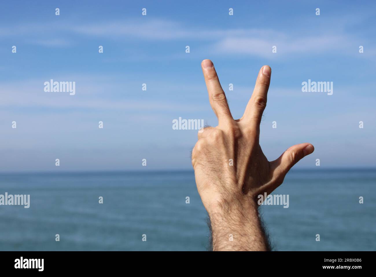 Hand doing,showing number three gesture symbol on blue summer sky ...
