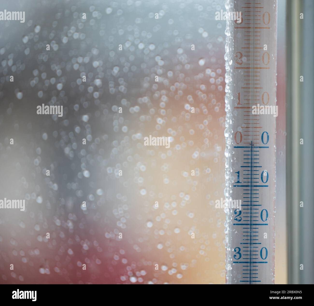 A window thermometer showing the outside temperature. Raindrops on the ...