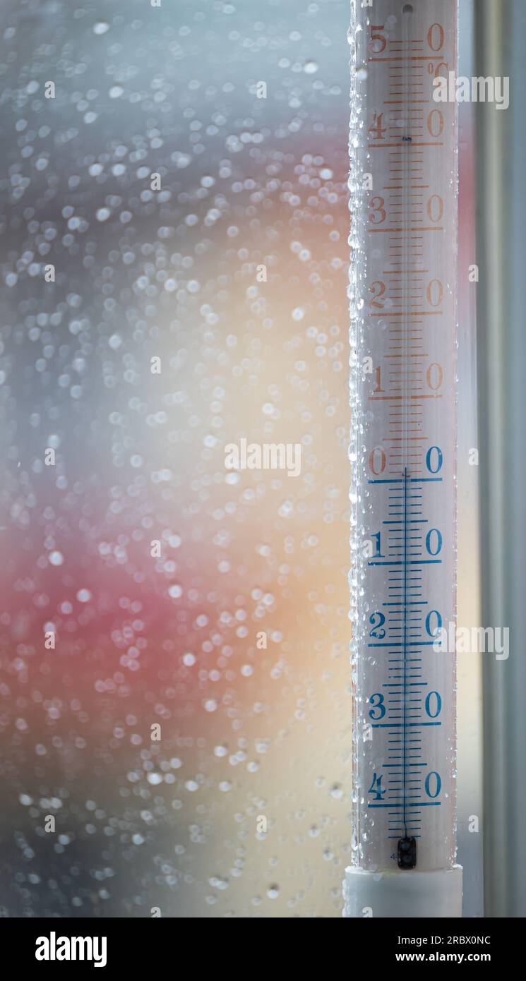A window thermometer showing the outside temperature. Raindrops on the ...