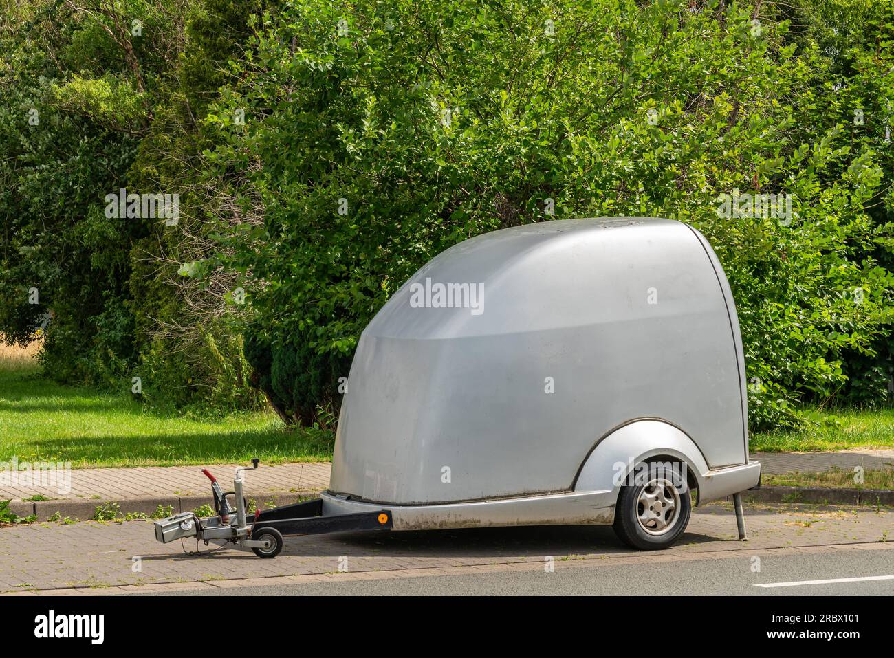 A small silver car trailer for transporting animals stands on the side ...