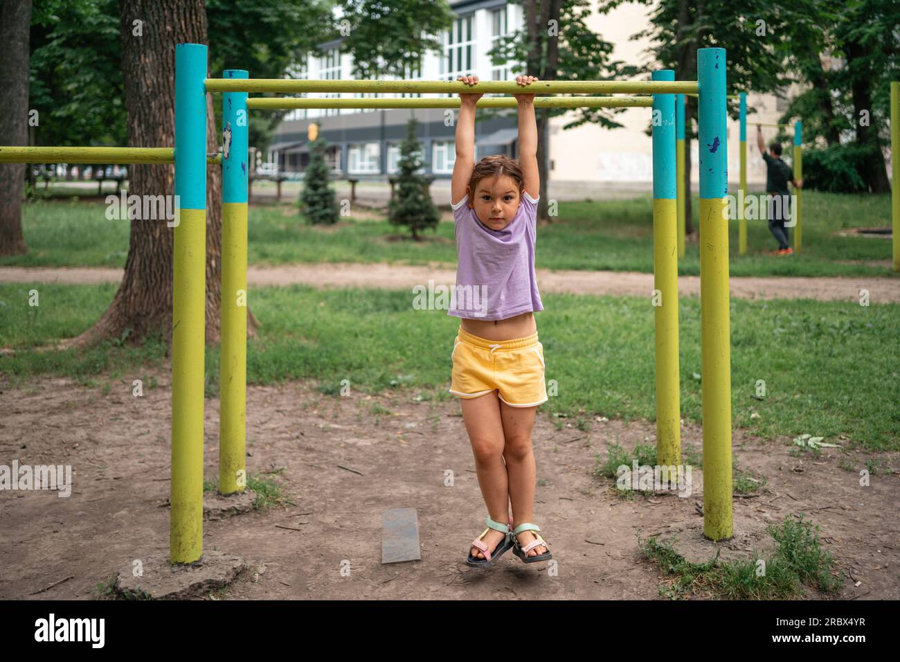 5 years old girl doing sports on the outdoors workout zone. Pull-ups on ...