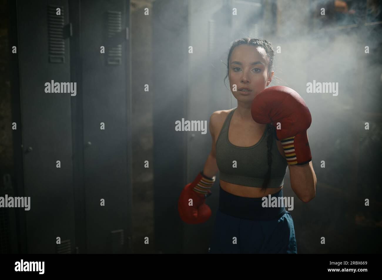 Portrait of tired sweaty female boxer standing in smoke looking at the ...