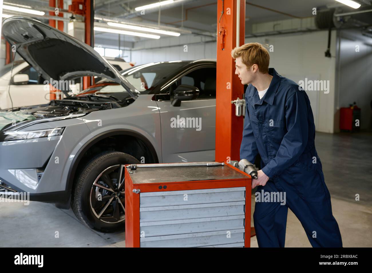 Male auto mechanic pushing wheeled tool kit box at car repair service ...