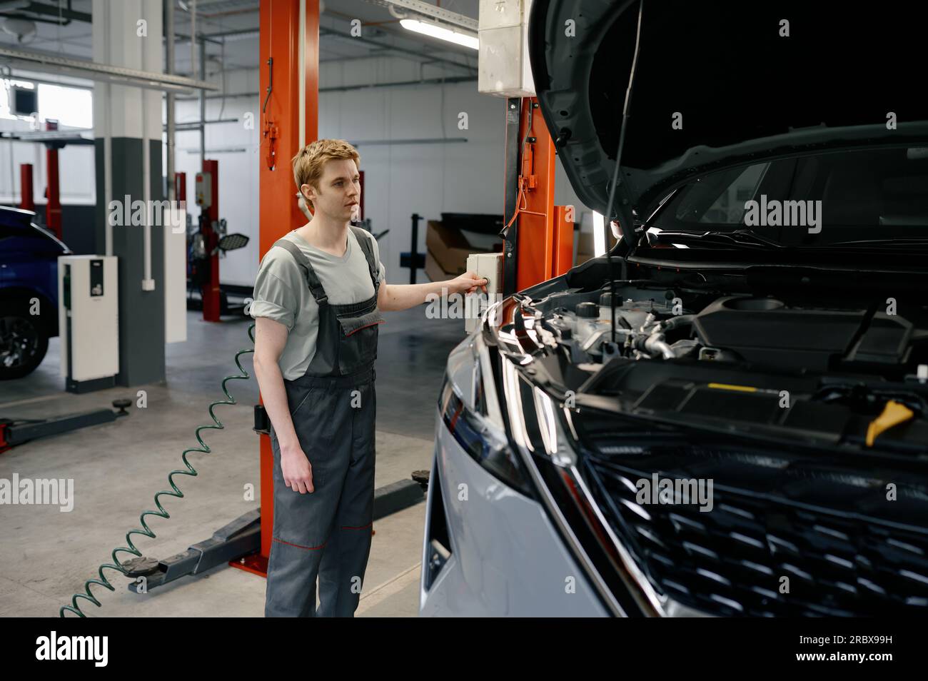 Young man mechanic raising broken car up on automated lifting machine ...