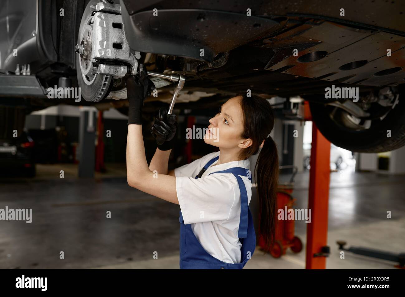 Woman mechanic fixing wheel hub or disc brake of raised car on lift ...