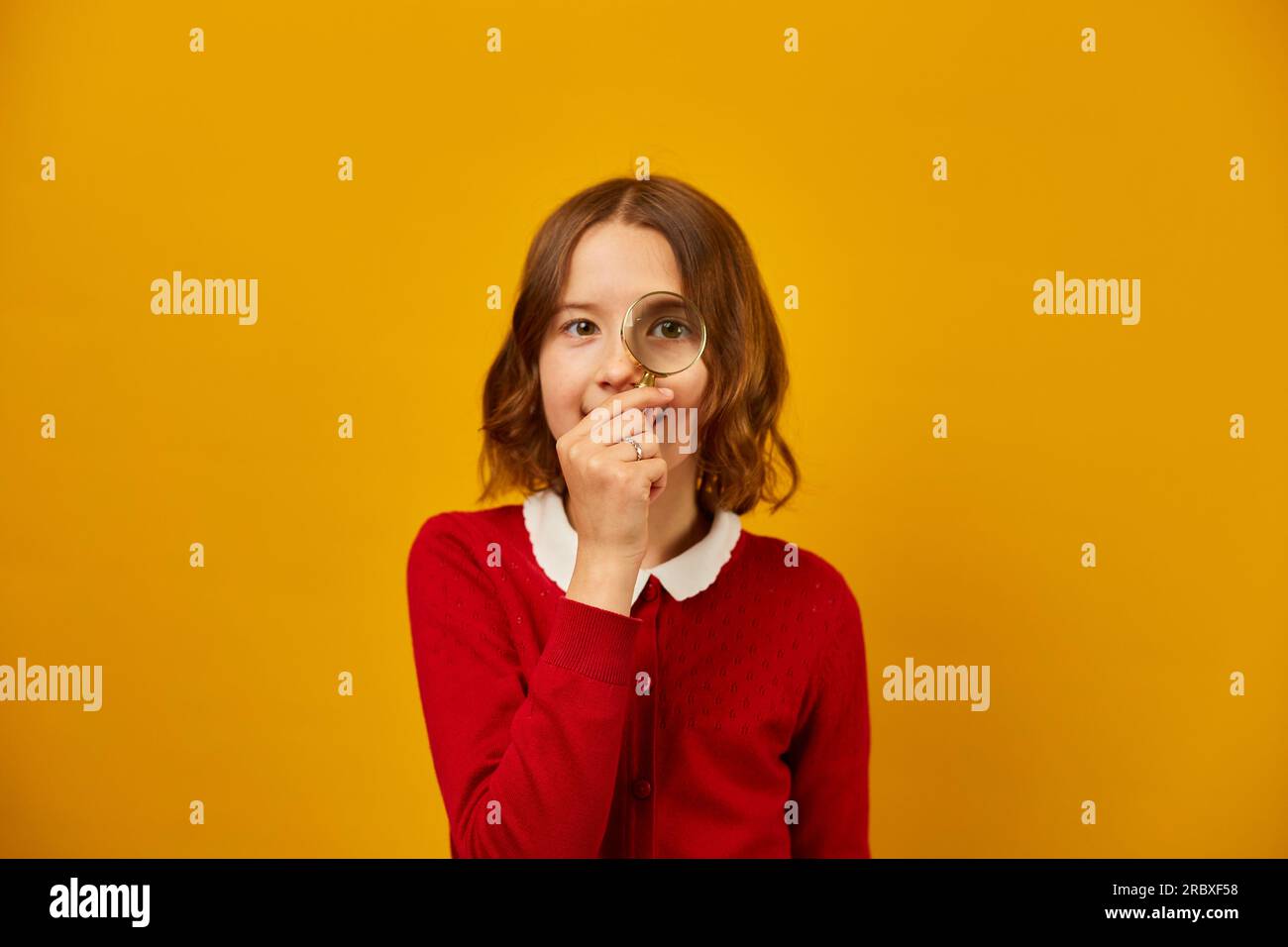 Stylish smiling school teenage girl holding magnifying glass on her eye ...