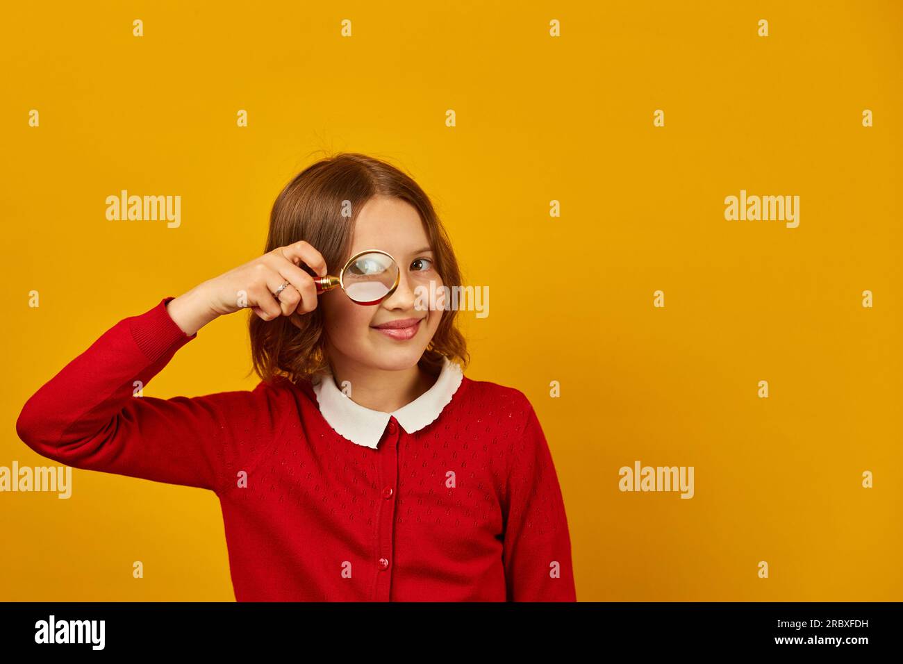 Stylish smiling school teenage girl holding magnifying glass on her eye ...