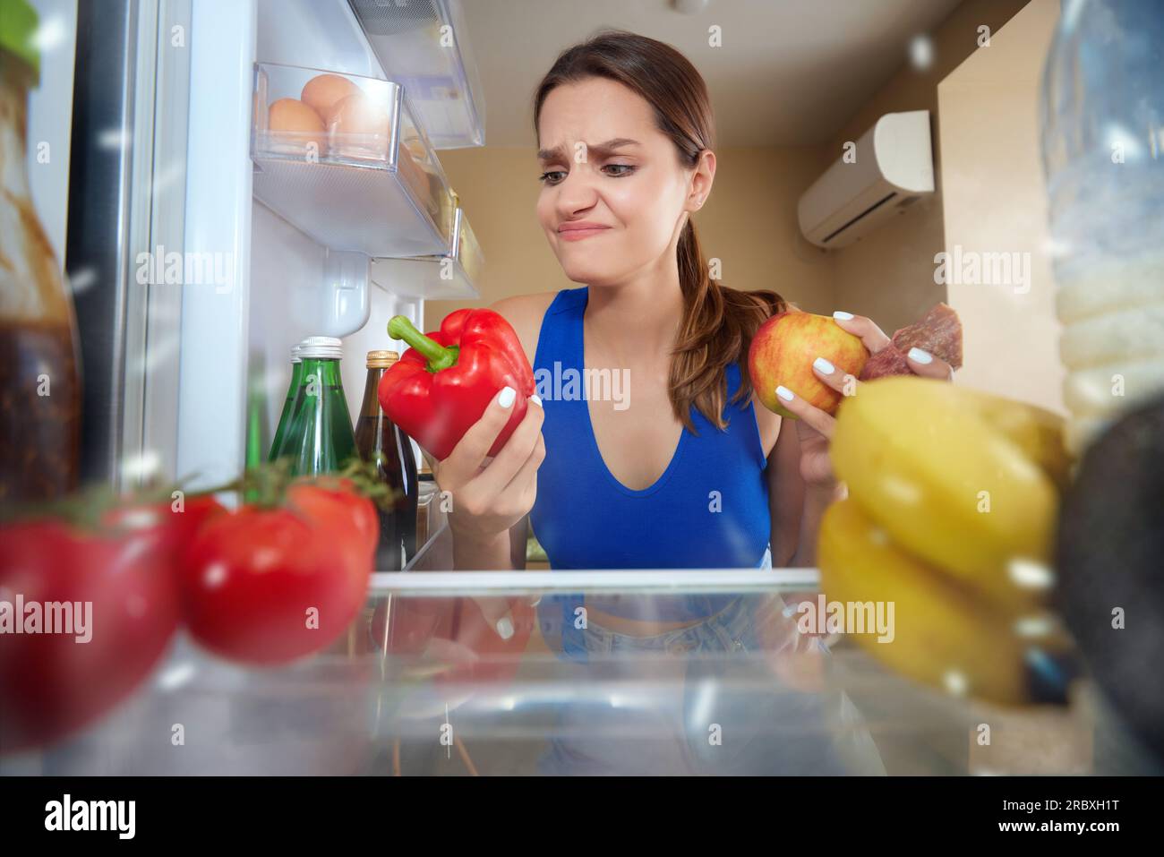 Young woman opening fridge, looking inside and emotionally choosing ...