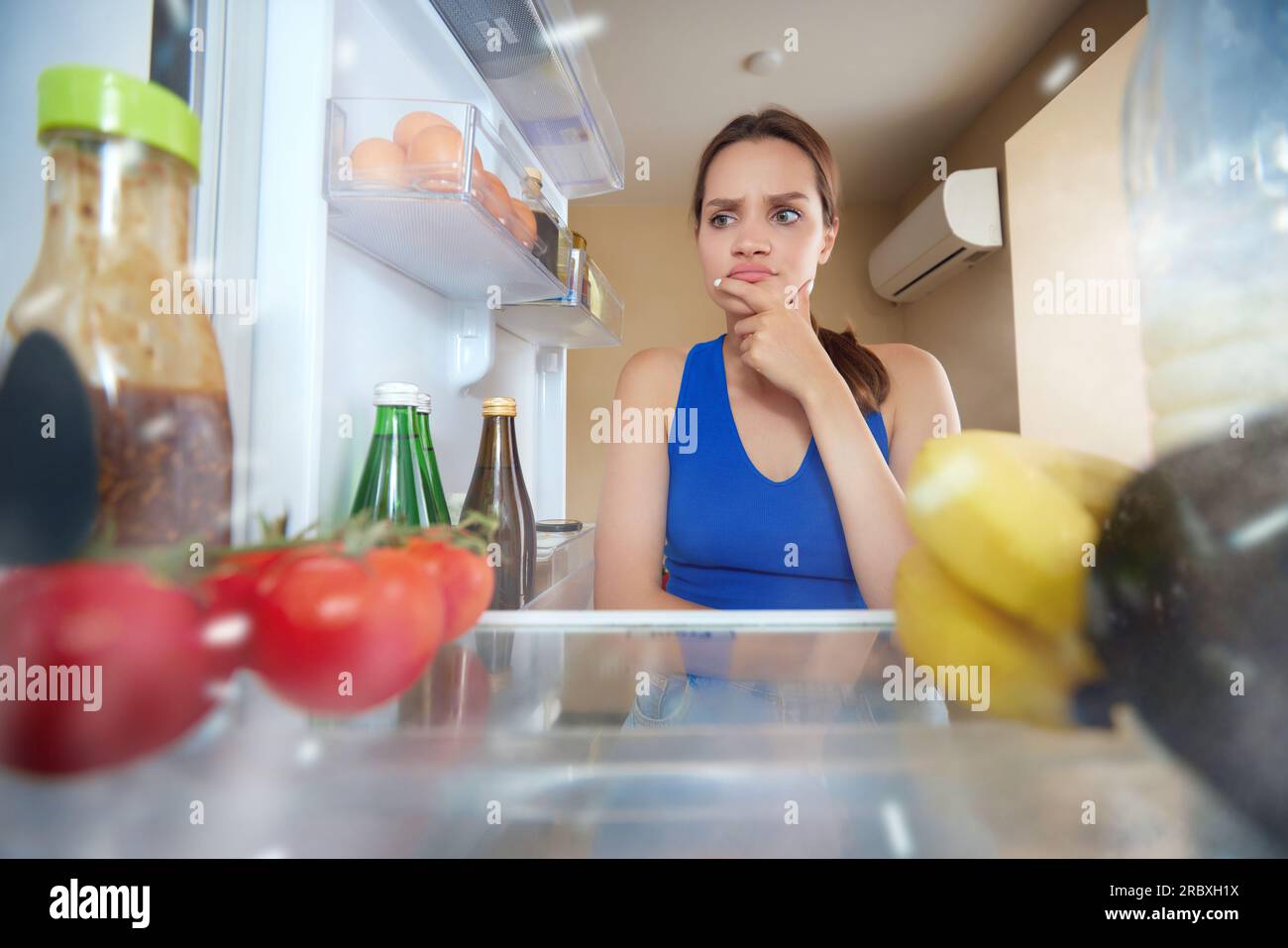 Young woman opening fridge, looking inside and choosing what to eat ...