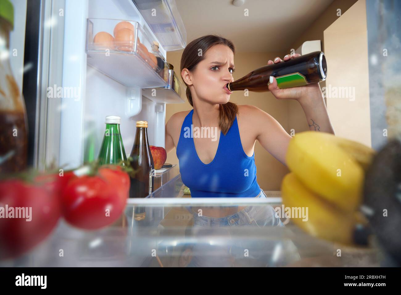 Young woman opening fridge, taking bottle and emotionally drinking ...
