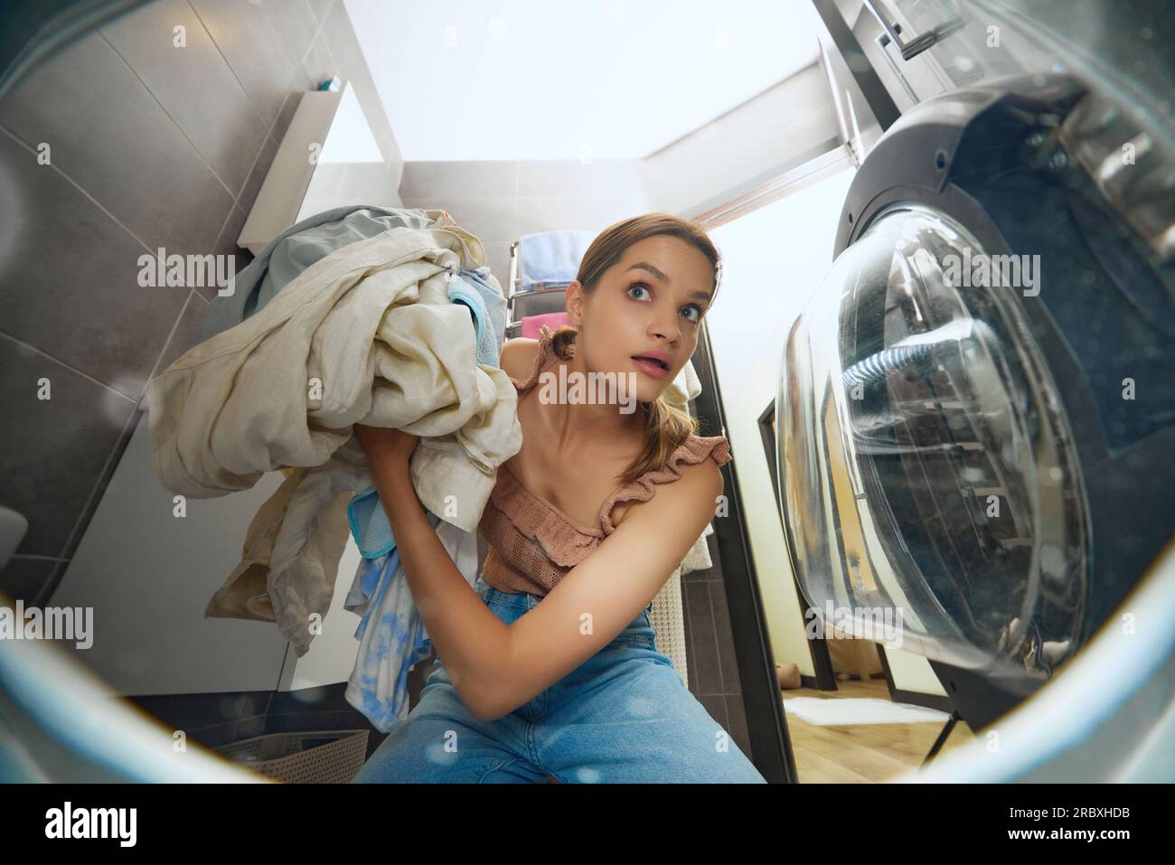 Young woman doing domestic chores, putting clothes into washer ...