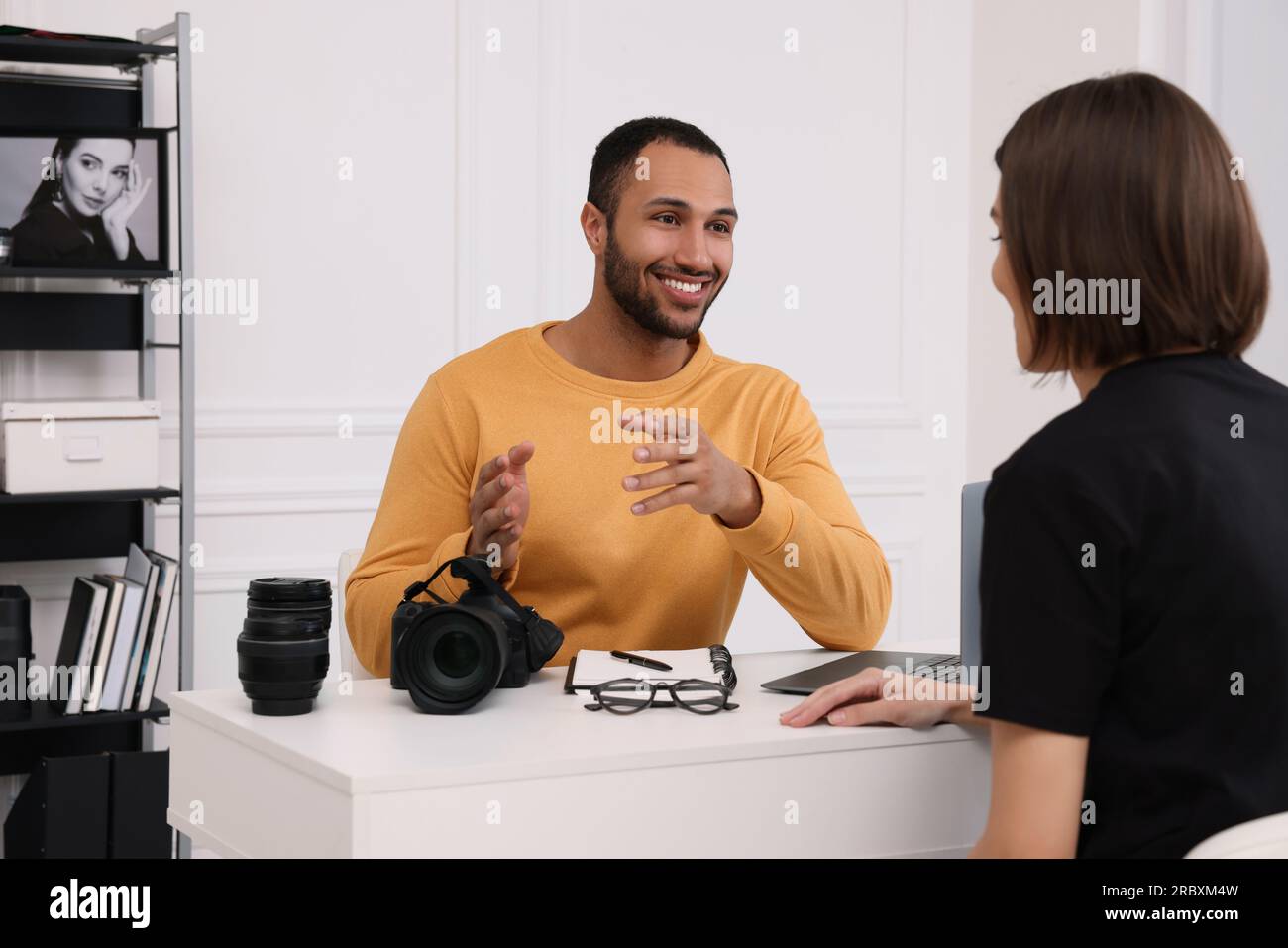 Young professional photographer with camera talking with woman in ...