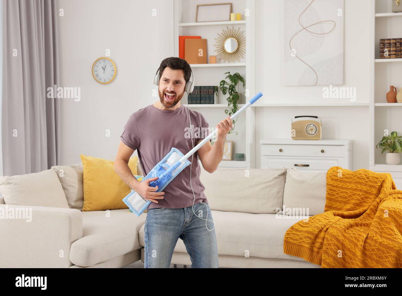 Spring cleaning. Man in headphones with mop singing while tidying up ...