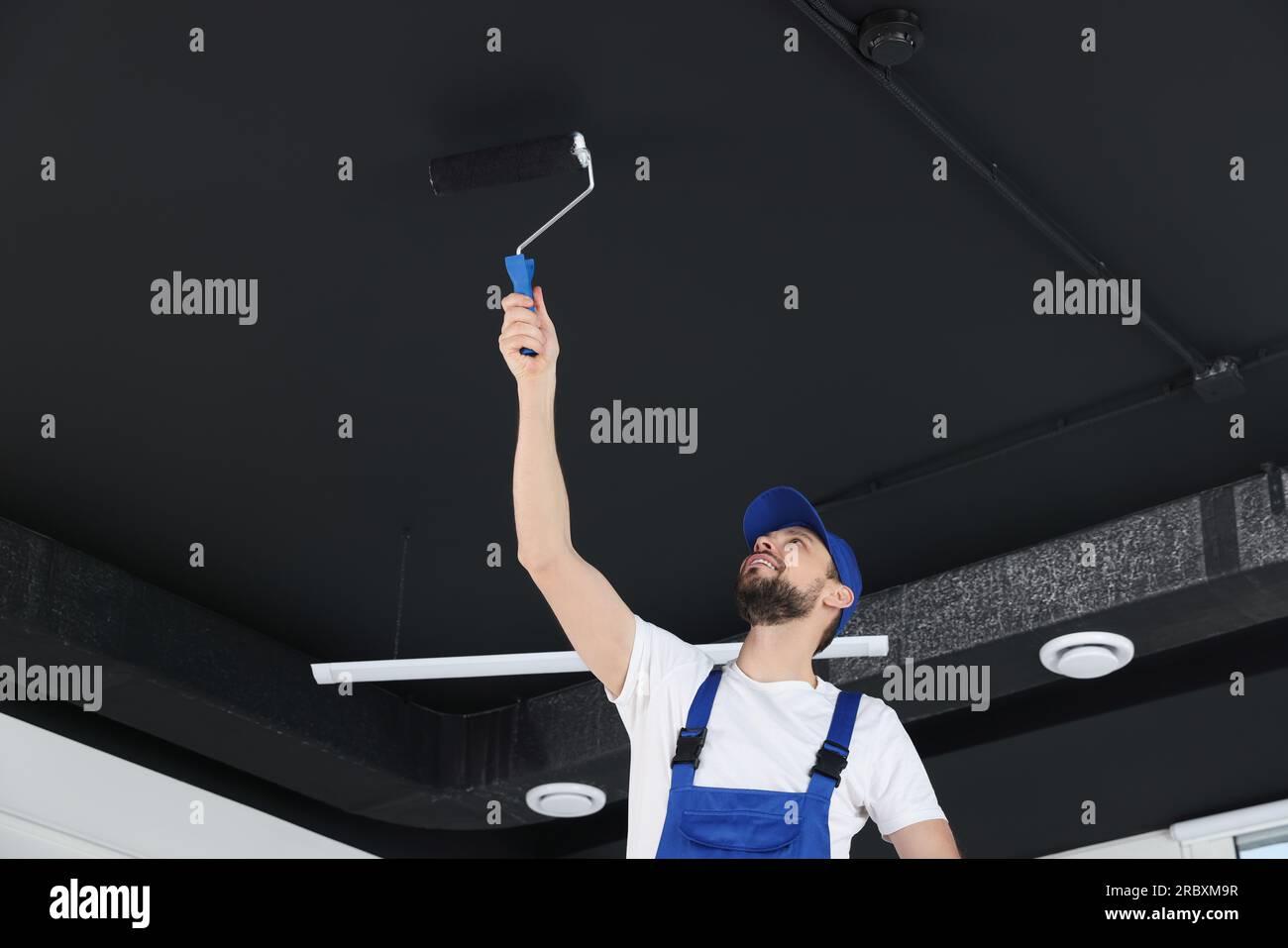 Worker in uniform painting ceiling with roller indoors Stock Photo - Alamy