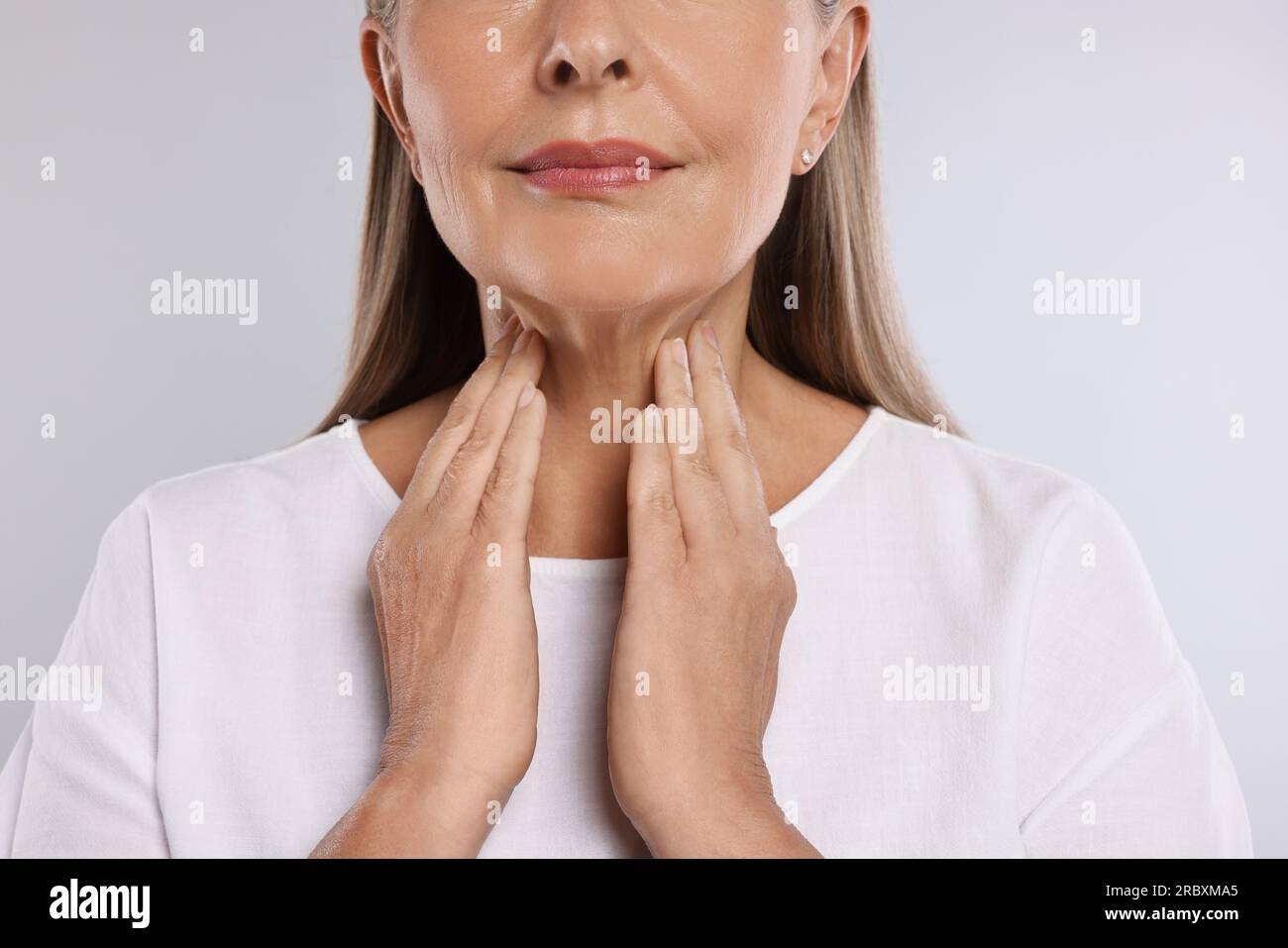 Endocrine system. Senior woman doing thyroid self examination on light ...