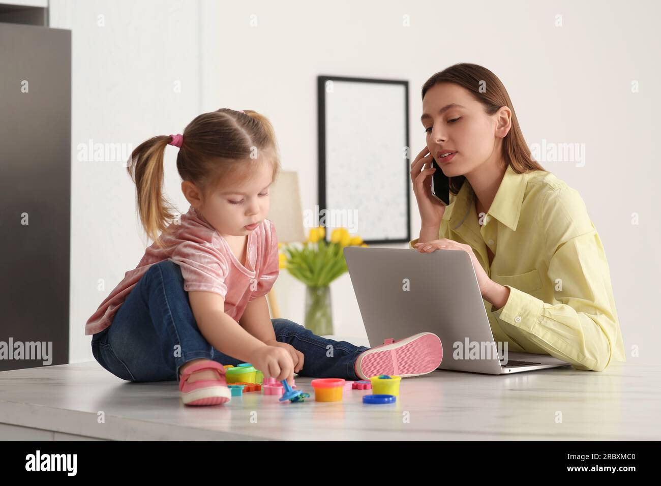 Woman working remotely at home. Busy mother watching over her daughter ...