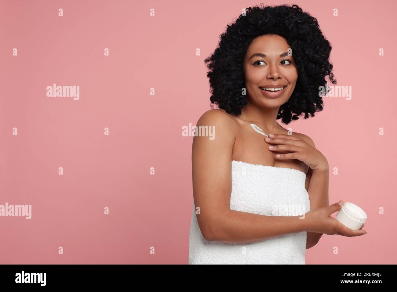 Young woman applying cream onto body on pink background. Space for text ...