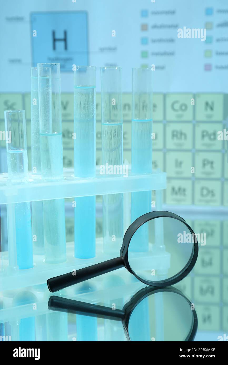 Magnifying glass and test tubes in rack on mirror surface against ...