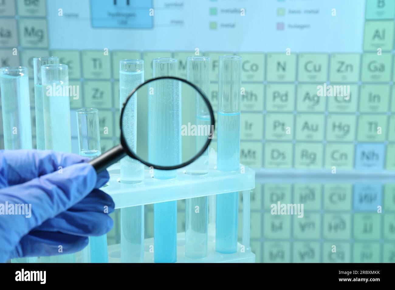 Laboratory assistant looking through magnifying glass on test tubes ...