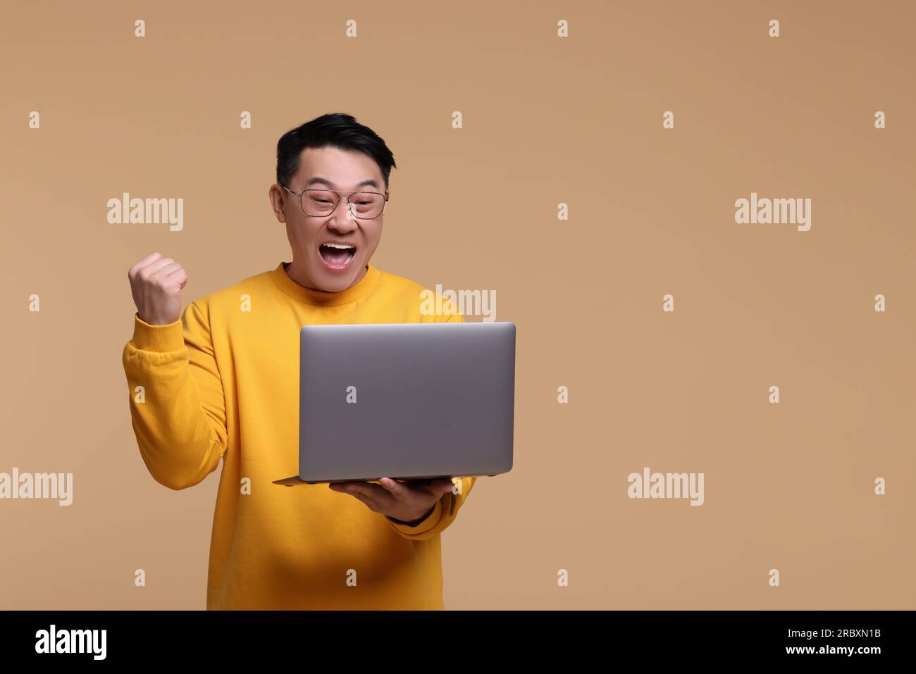 Emotional man with laptop on beige background, space for text Stock ...