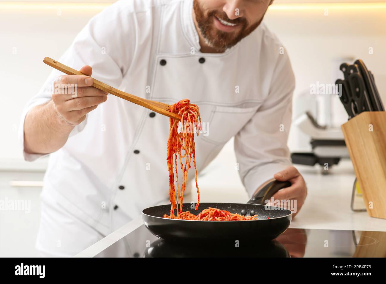 Professional chef cooking delicious spaghetti in frying pan indoors ...