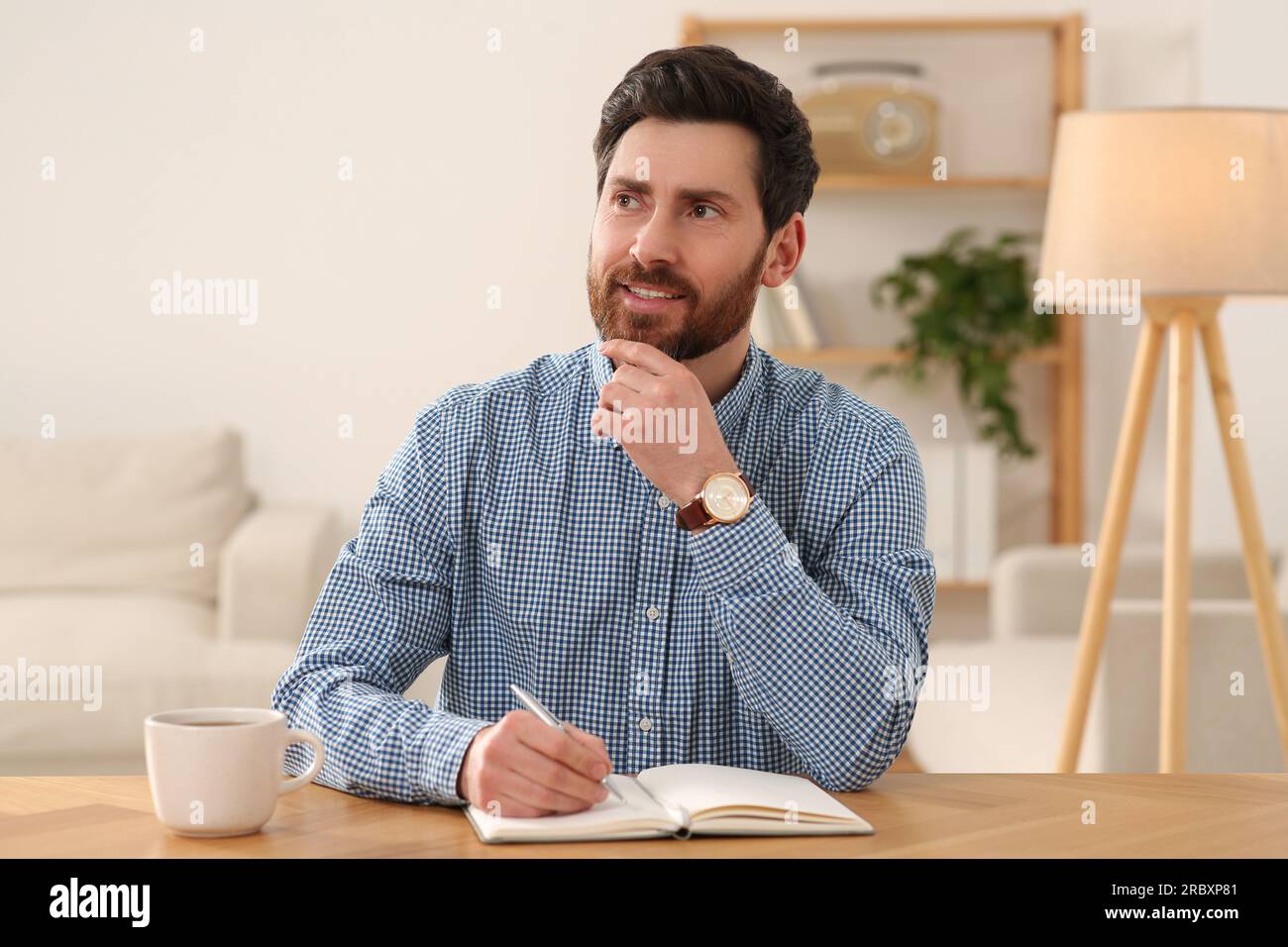 Happy man taking notes during video call at wooden desk indoors, view ...