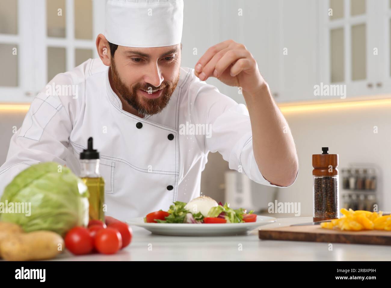 Professional chef salting delicious salad at marble table in kitchen ...