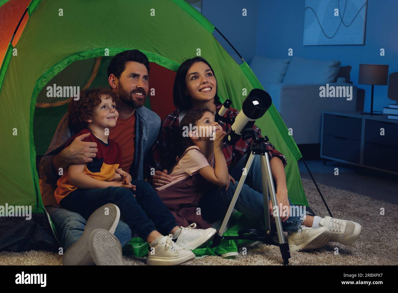 Happy family using telescope to look at stars while sitting in camping ...