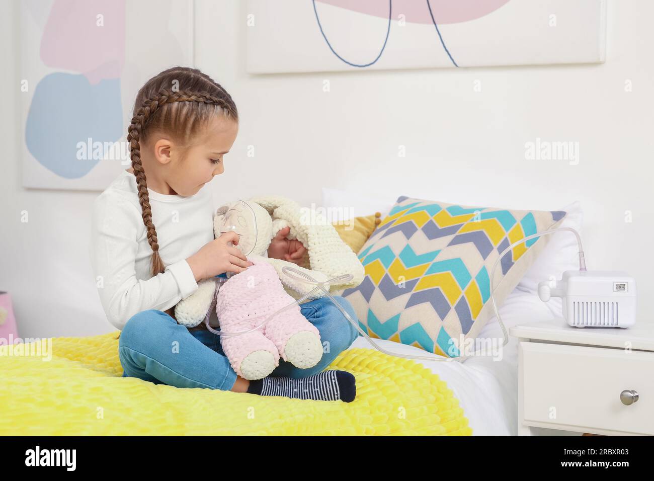Little girl with toy bunny and nebulizer for inhalation on bed at home ...