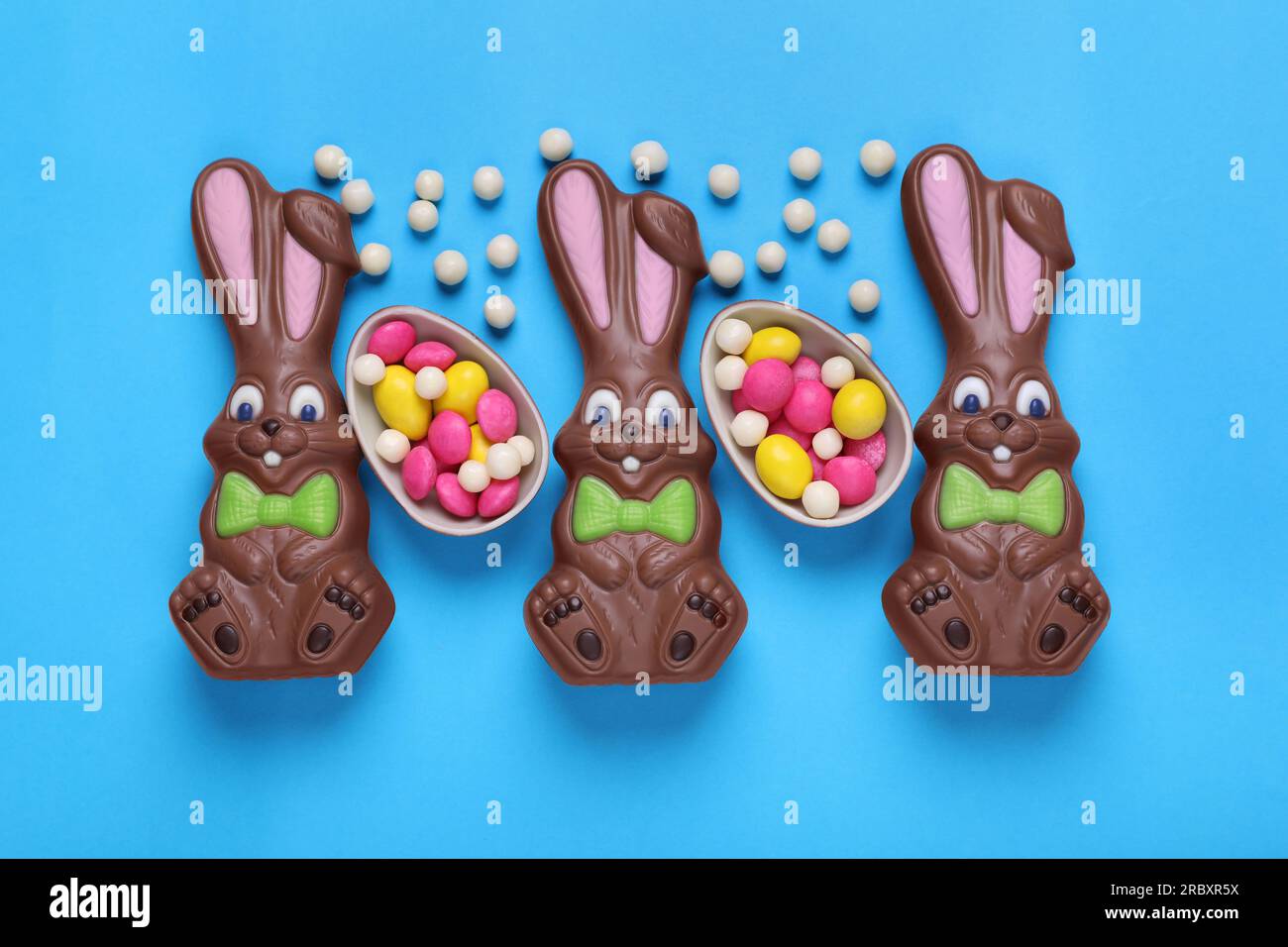 Chocolate Easter bunnies, halves of egg and candies on light blue ...