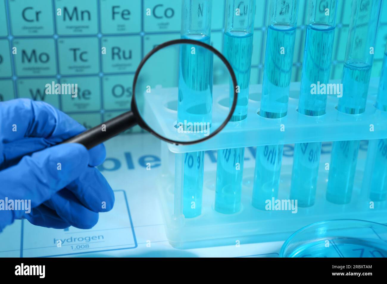 Scientist with magnifying glass examining test tube against periodic ...