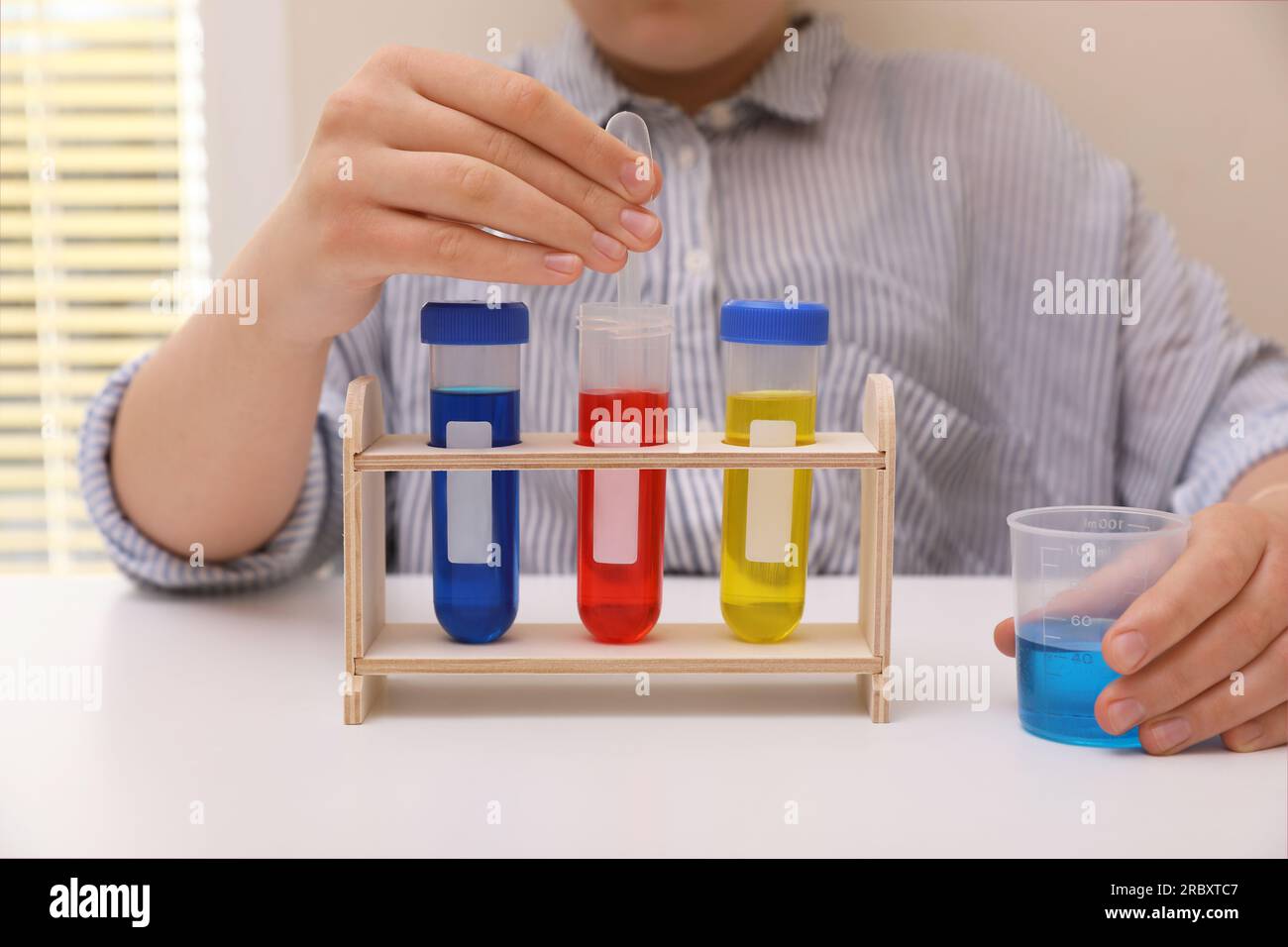 Girl with colorful liquids in test tubes and beaker at white table ...