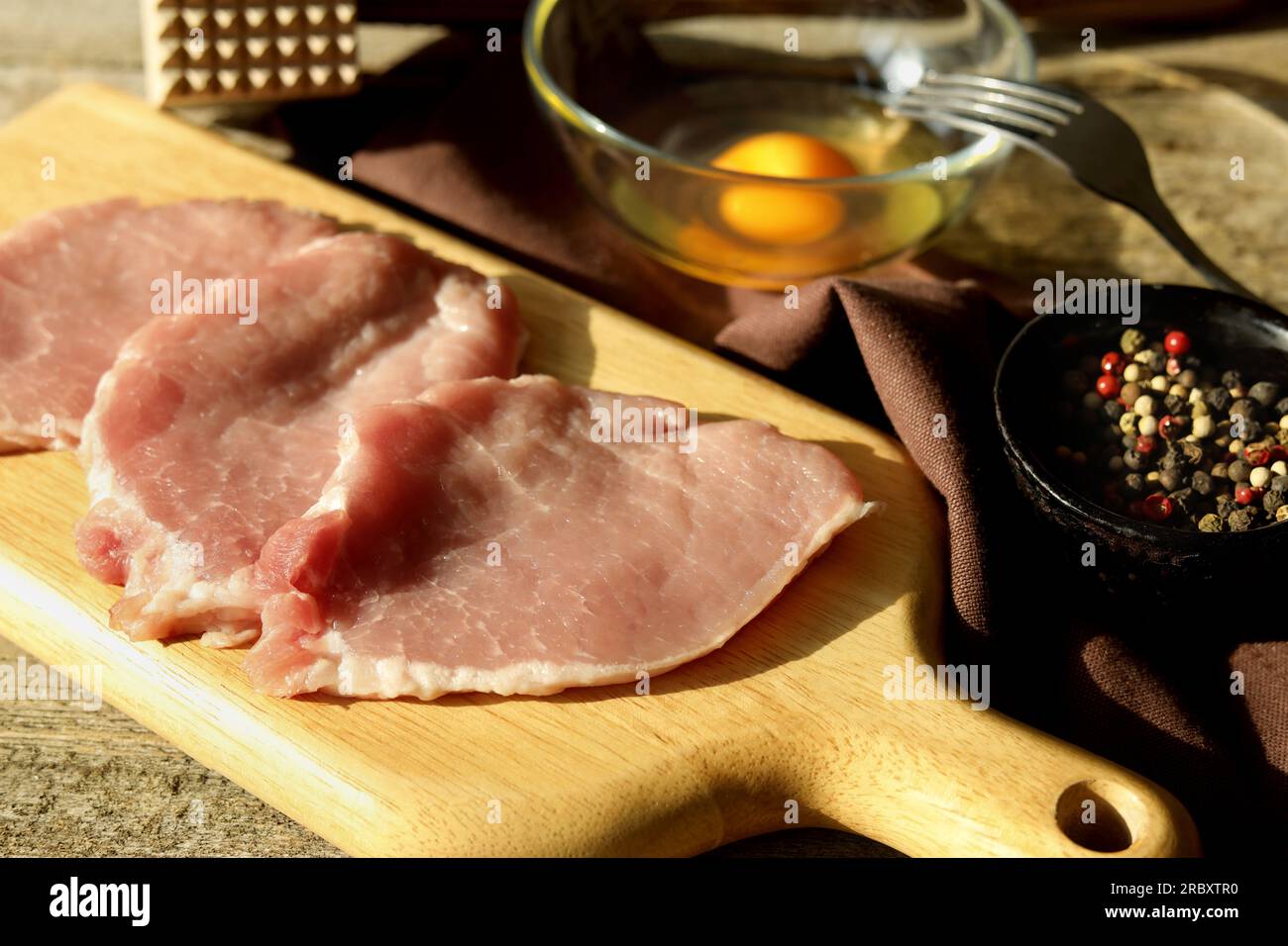 Cooking schnitzel. Raw pork slices, egg and peppercorns on table ...