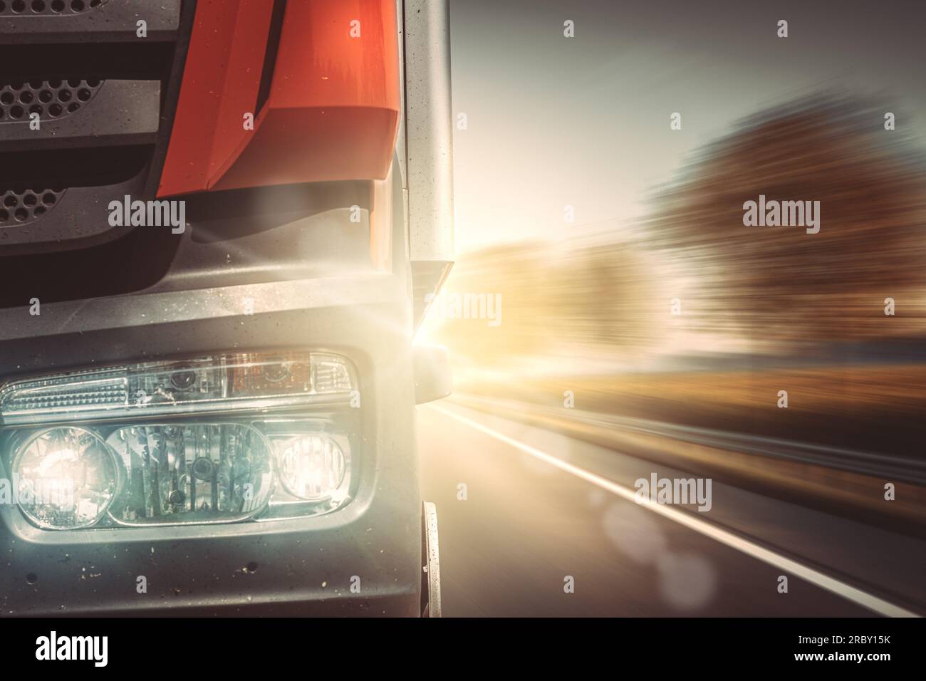Front of fast moving truck with lights on on country road with sun rays ...
