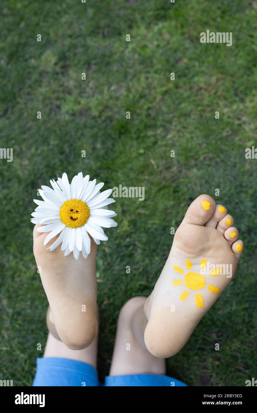 Chamomile flower between toes of bare foot and painted sun on other ...